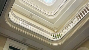 Um interior com vários níveis, claraboia central, balaústres brancos e uma escadaria.