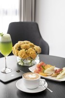 Uma mesa com uma xícara de café, um copo de bebida verde, um prato de comida e um laptop.