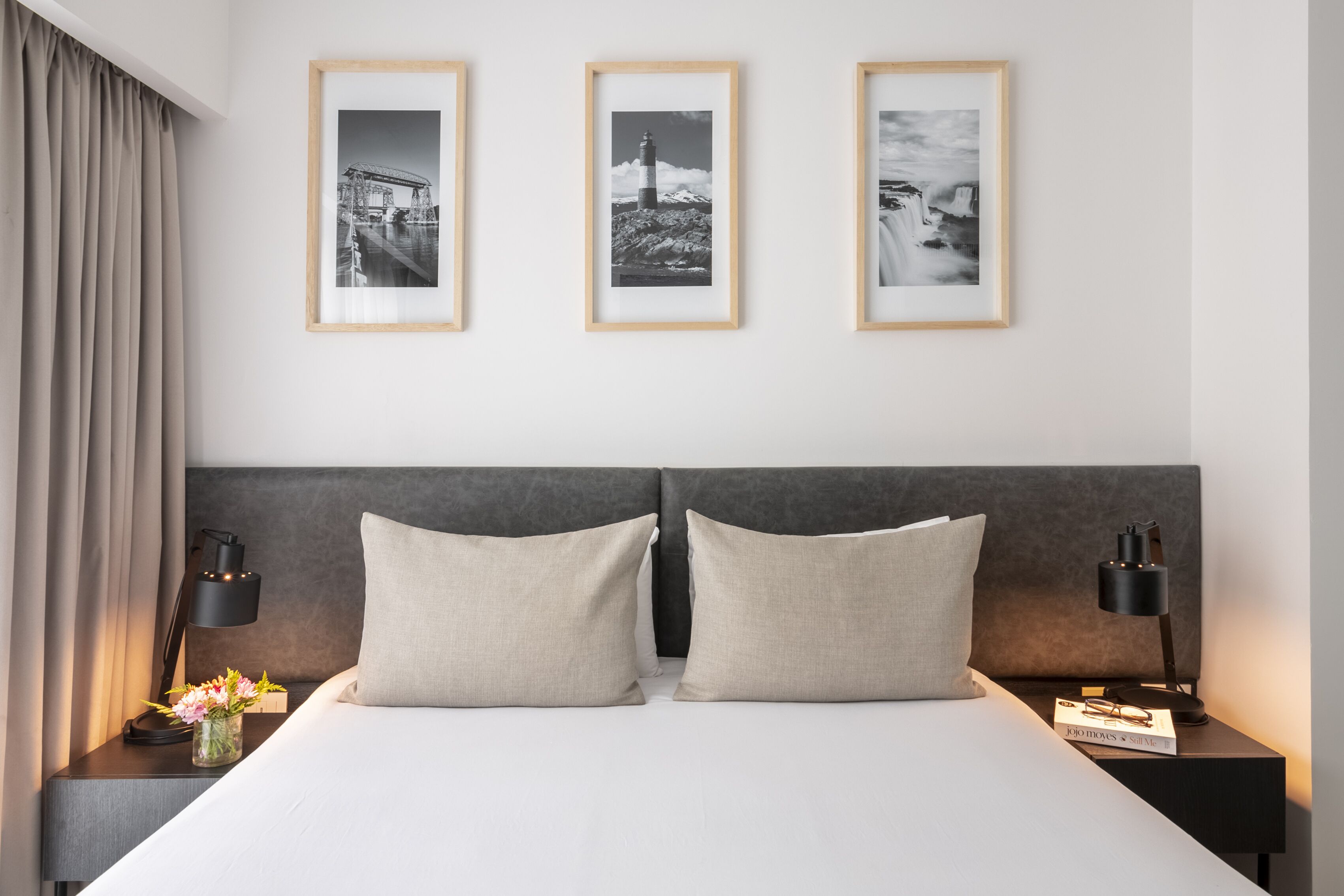 Quarto bem arrumado com uma cama, duas mesas de cabeceira e três quadros na parede.
