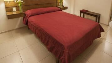 Uma cama bem arrumada com um cobreleto vermelho, duas mesas de cabeceira com abajures e um pequeno banco.