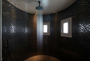 Casa de banho com paredes em mosaico, chuveiro com teto circular e duas janelas.