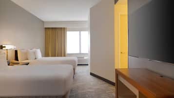 Quarto de hotel com duas camas, uma escrivaninha, televisão de tela plana e uma janela grande com cortinas.
