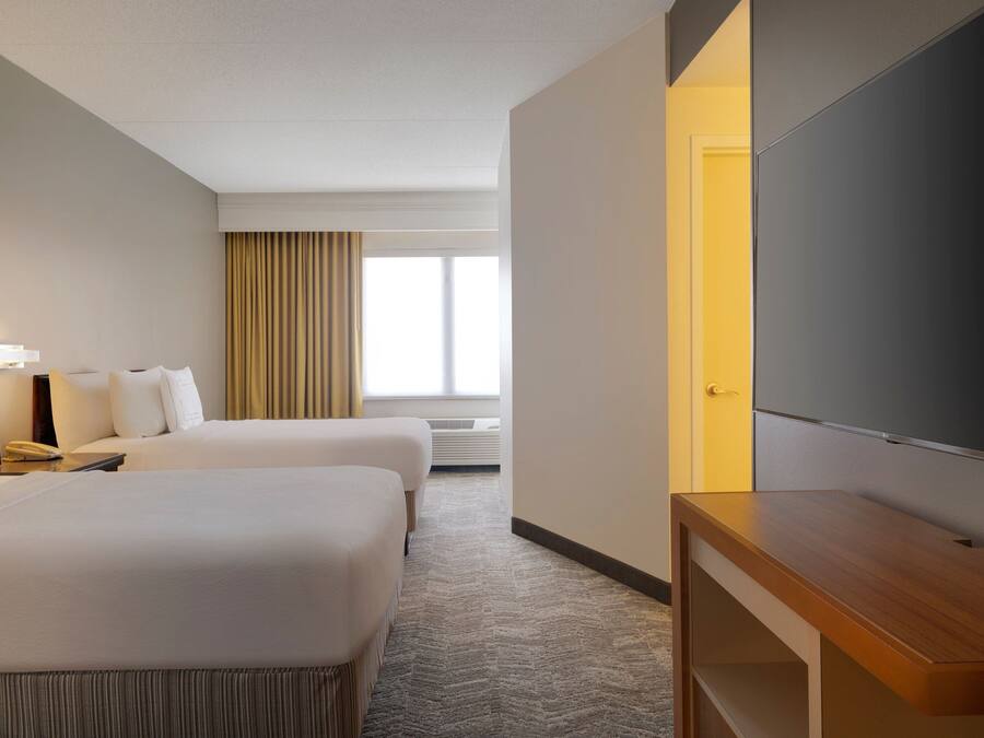 Quarto de hotel com duas camas, uma escrivaninha, televisão de tela plana e uma janela grande com cortinas.