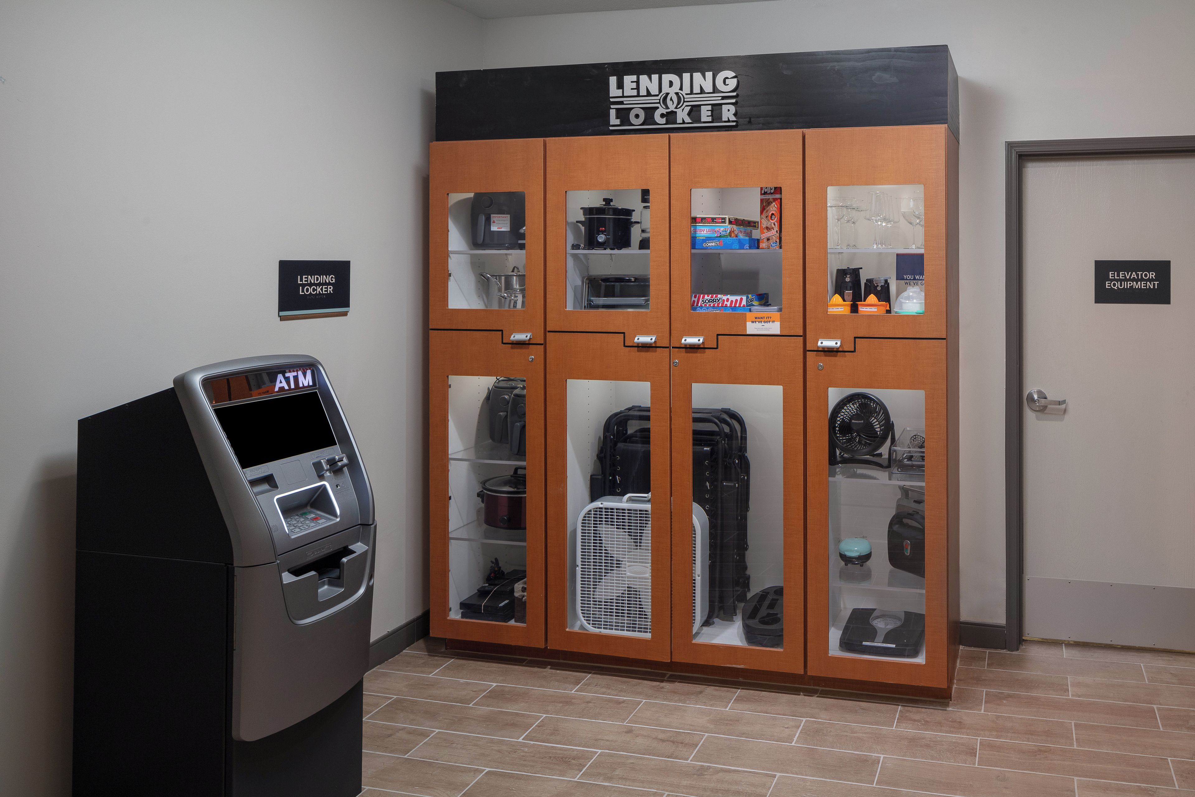 Um armário para empréstimos com uma placa acima, um caixa eletrônico e uma porta com a inscrição 'Equipamentos de Elevador'.
