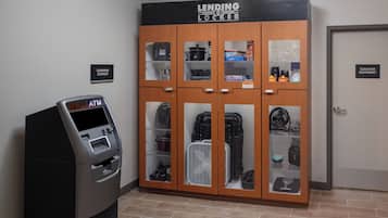 Um armário para empréstimos com uma placa acima, um caixa eletrônico e uma porta com a inscrição 'Equipamentos de Elevador'.