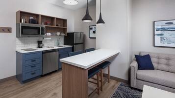 Cozinha moderna com ilha central, eletrodomésticos embutidos e área de refeições com sofá e cadeiras.
