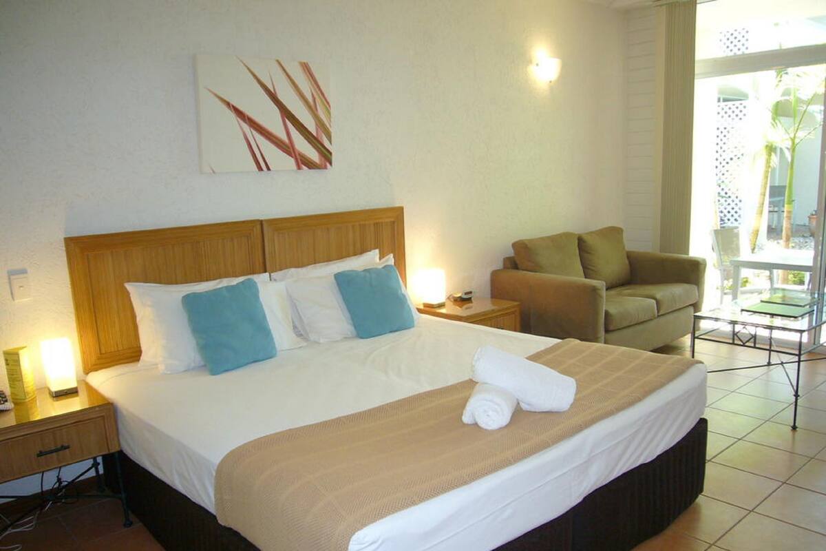 Quarto de hotel com uma cama grande, mesa de cabeceira, uma cadeira e vista para o exterior.
