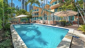 Piscina com superfície de água azul cristalina, rodeada por palmeiras e um edifício com varandas.