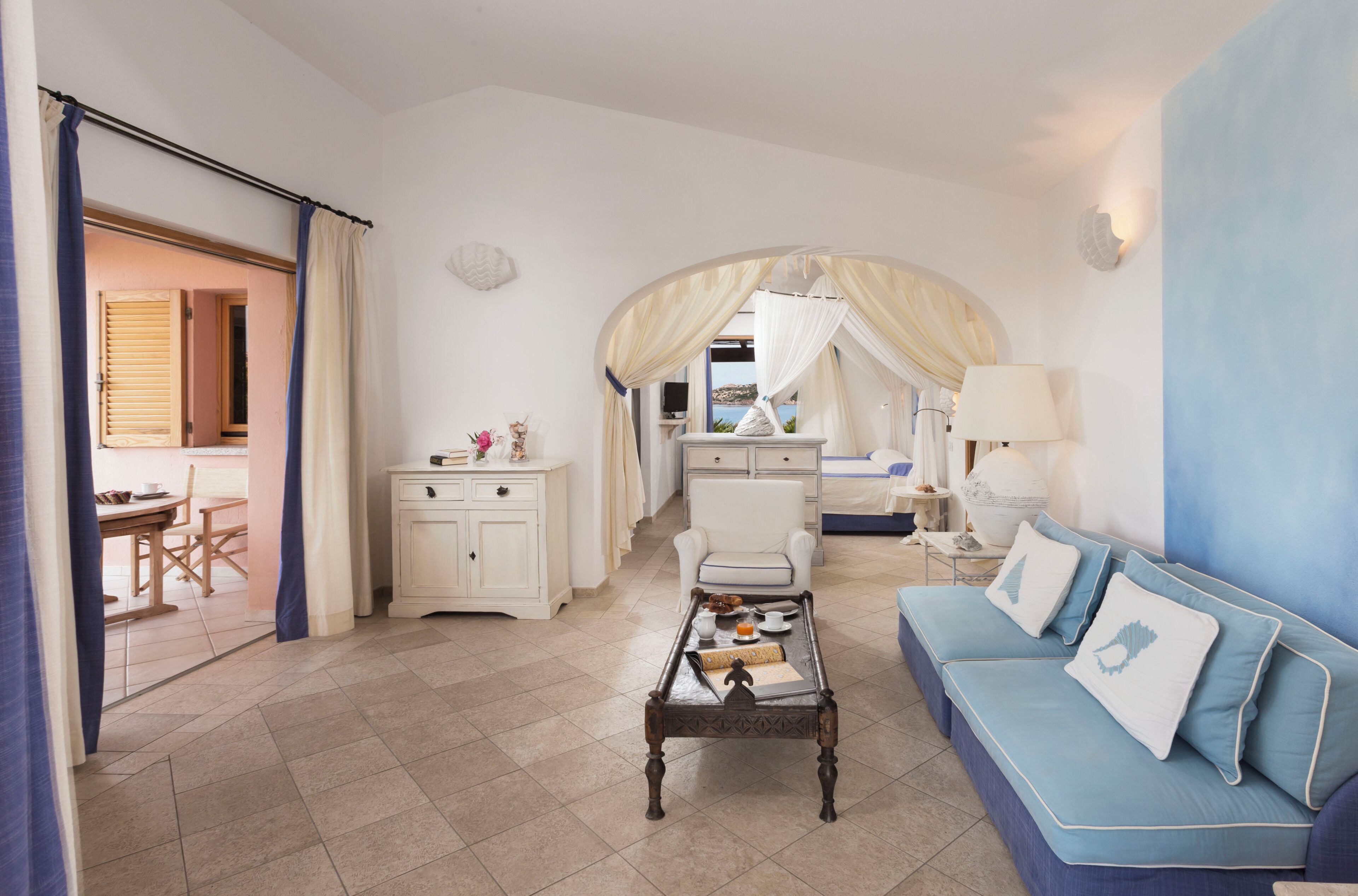 Quarto de hotel com área de refeições, um sofá, uma mesa de centro e vista para o mar.