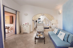 Quarto de hotel com área de refeições, um sofá, uma mesa de centro e vista para o mar.