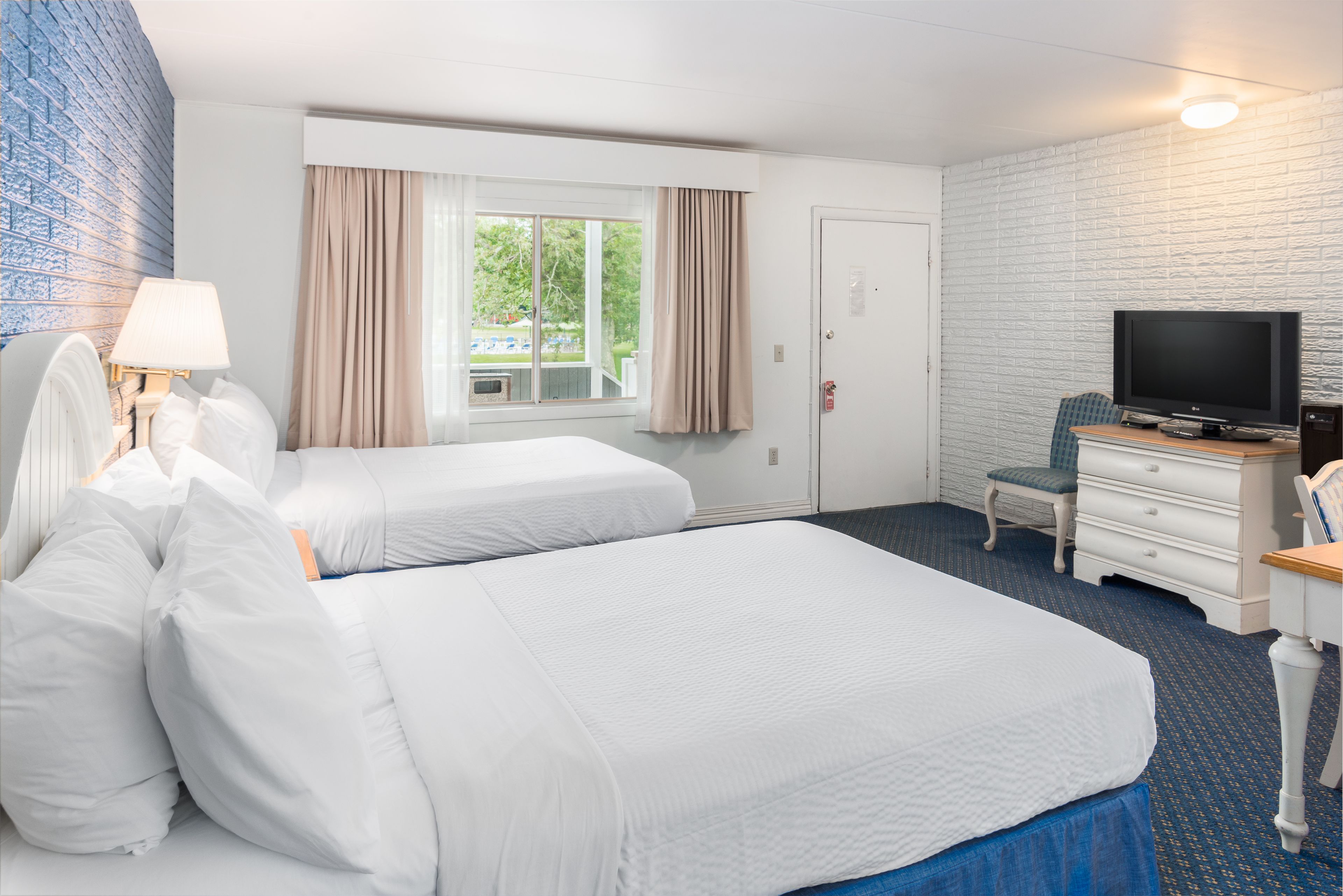 Quarto de hotel com duas camas, televisão, secretária e janela com cortinas.