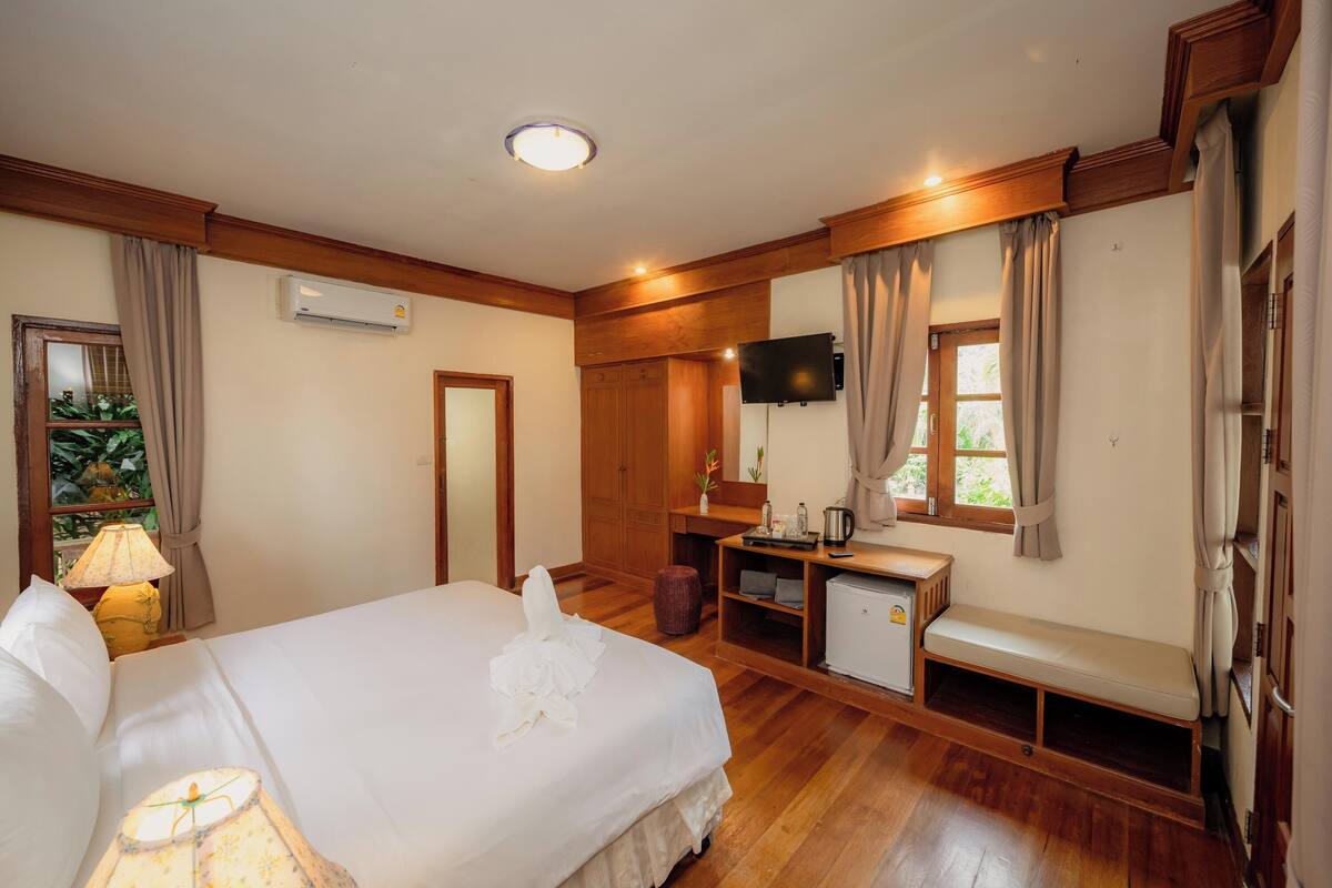 Quarto de hotel com cama, luminária de cabeceira, ar condicionado, televisão e uma pequena escrivaninha com cadeira.