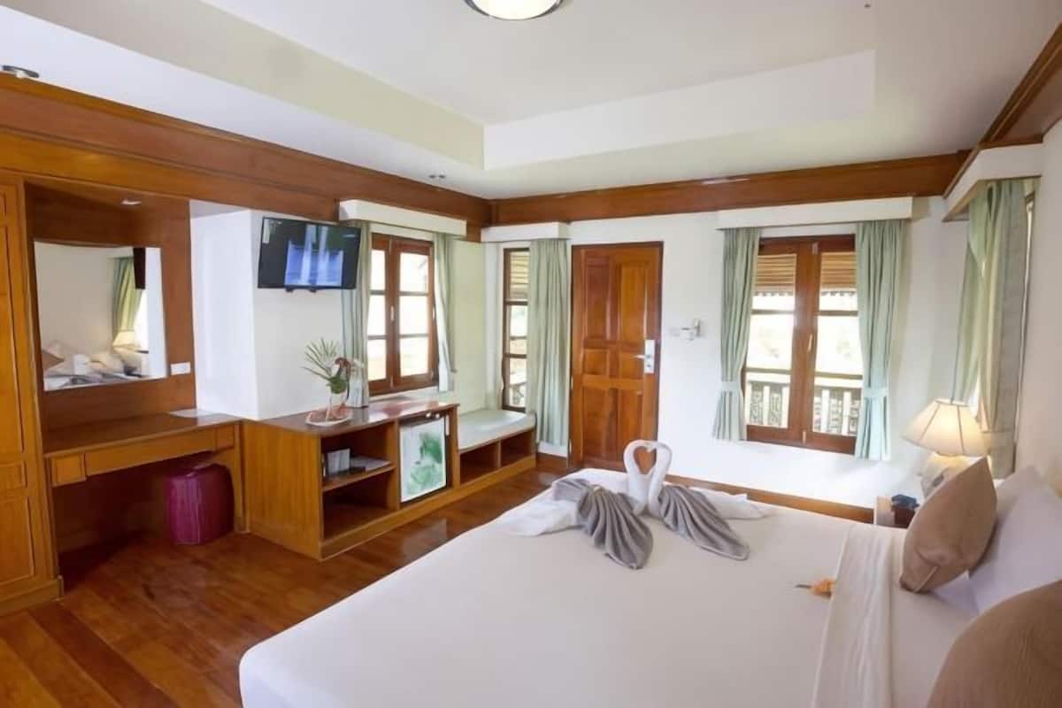 Quarto de hotel com uma cama grande, uma escrivaninha, uma televisão e uma janela com cortinas.