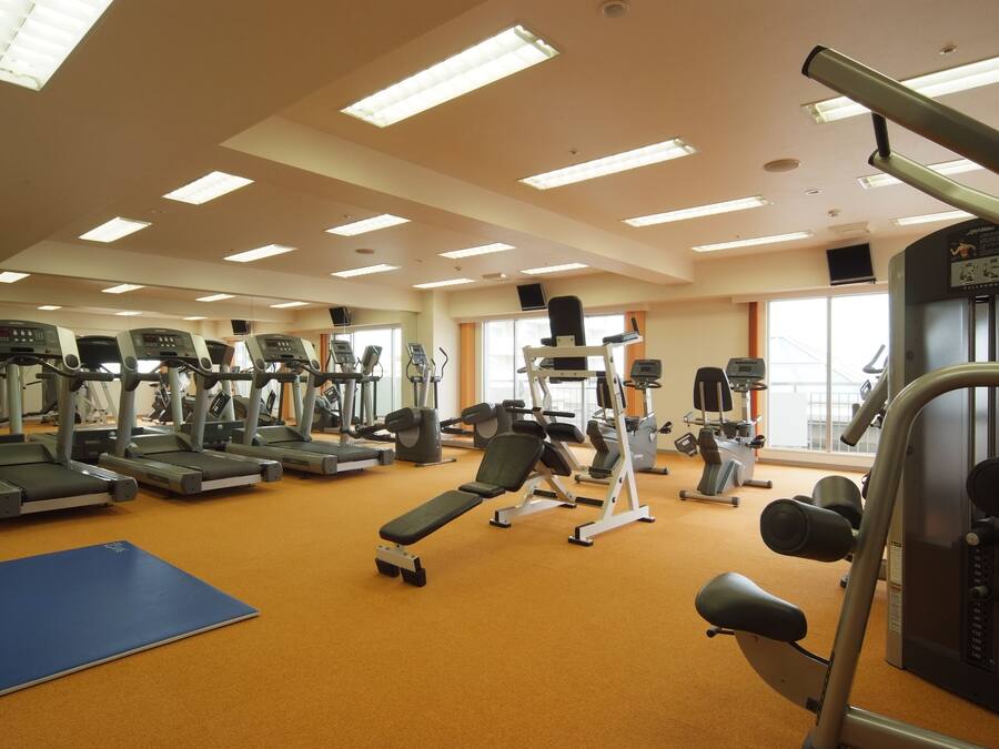Uma academia com esteiras, um banco e diversos equipamentos de exercícios.