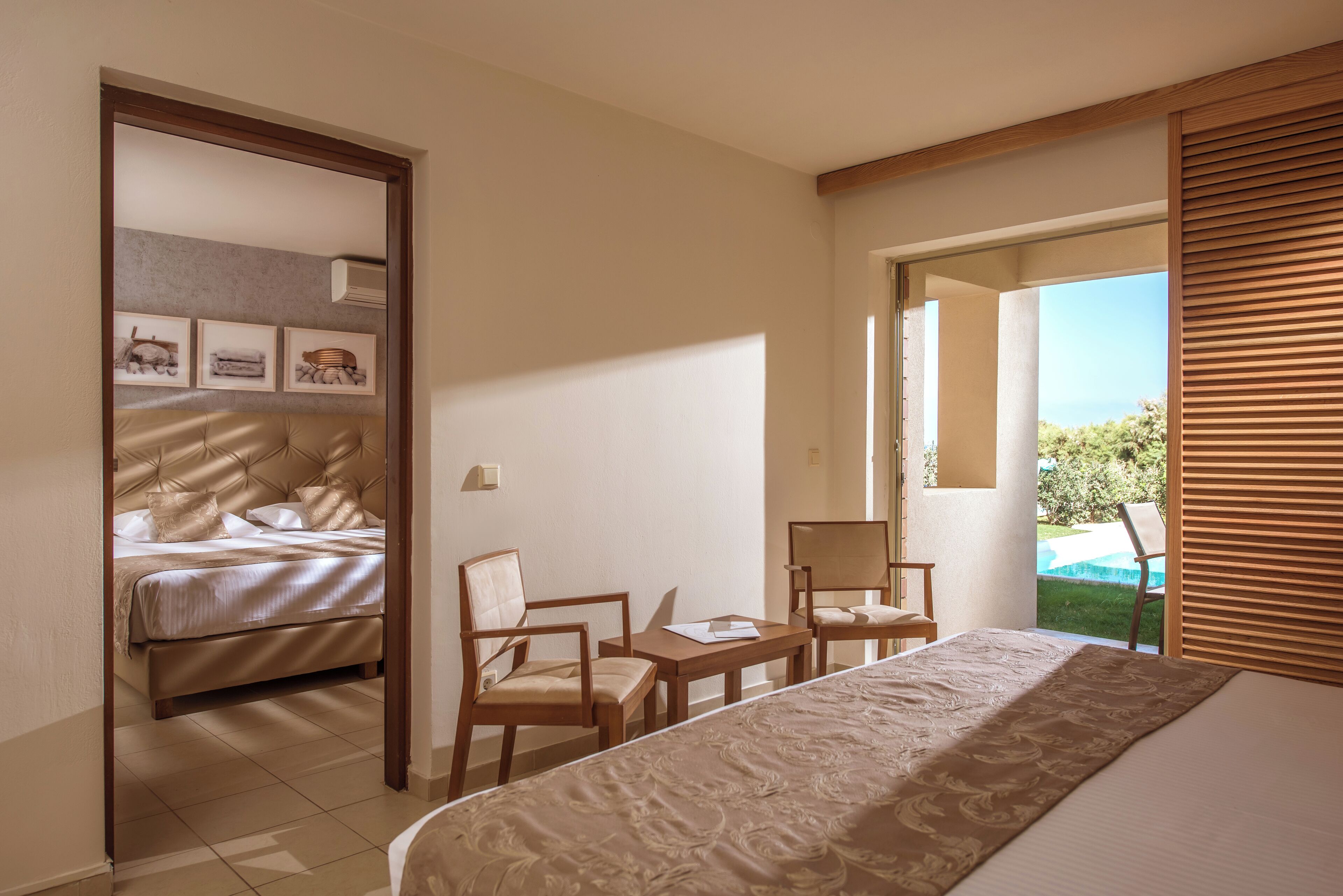 Quarto de hotel com uma cama, duas cadeiras, uma mesa pequena e vista para o exterior.