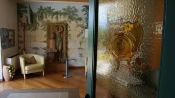 Quarto com piso de madeira, uma poltrona bege, uma mesinha e uma parede decorativa com um mural.