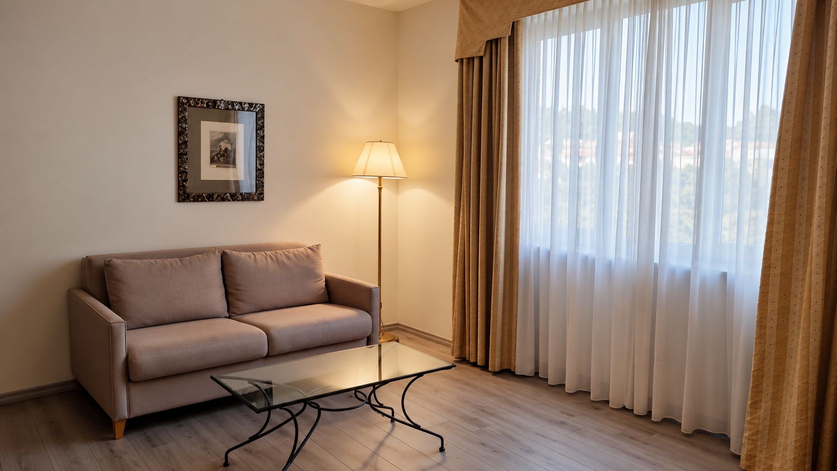 Quarto com sofá, mesa de centro de vidro, abajur e cortinas leves.