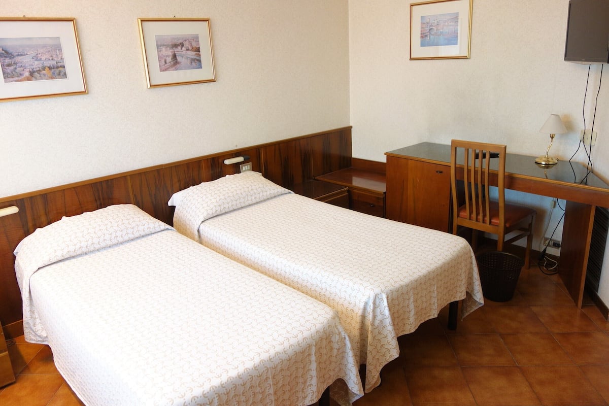 Quarto de hotel com duas camas, uma escrivaninha, uma cadeira e uma televisão.