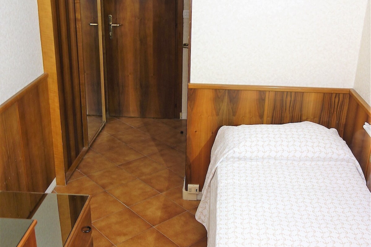 Quarto com guarda-roupa de madeira, cama com colcha estampada e chão de azulejos.