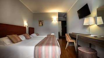 Quarto de hotel com duas camas, uma escrivaninha, uma cadeira, uma televisão e um abajur.
