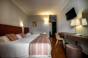 Quarto de hotel com duas camas, uma escrivaninha, uma cadeira, uma televisão e um abajur.