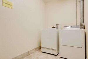 Uma área de lavanderia com duas máquinas de lavar roupa brancas e uma placa com a inscrição 'GUEST LAUNDRY'.