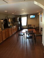 Uma cozinha espaçosa com armários de madeira, um espaço de jantar com mesa e cadeiras, uma geladeira e uma TV de tela plana na parede.