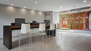 Uma área de recepção com um balcão, dois computadores e quatro cadeiras brancas.