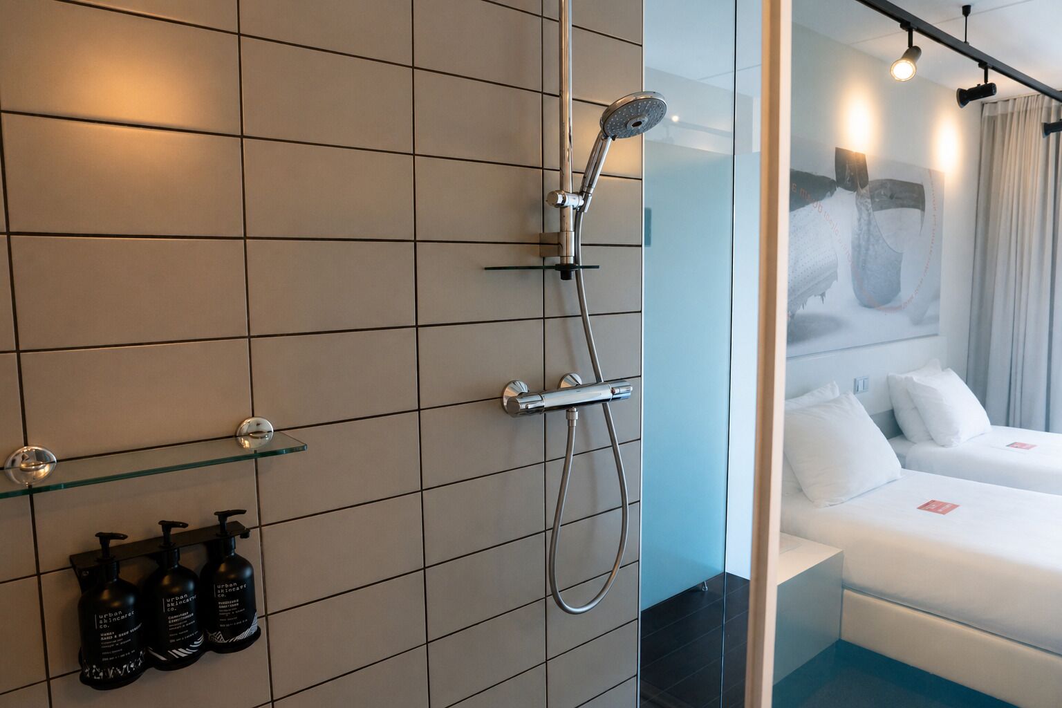 Um banheiro moderno com chuveiro, uma prateleira de vidro com artigos de higiene pessoal e uma cama com roupa de cama branca.