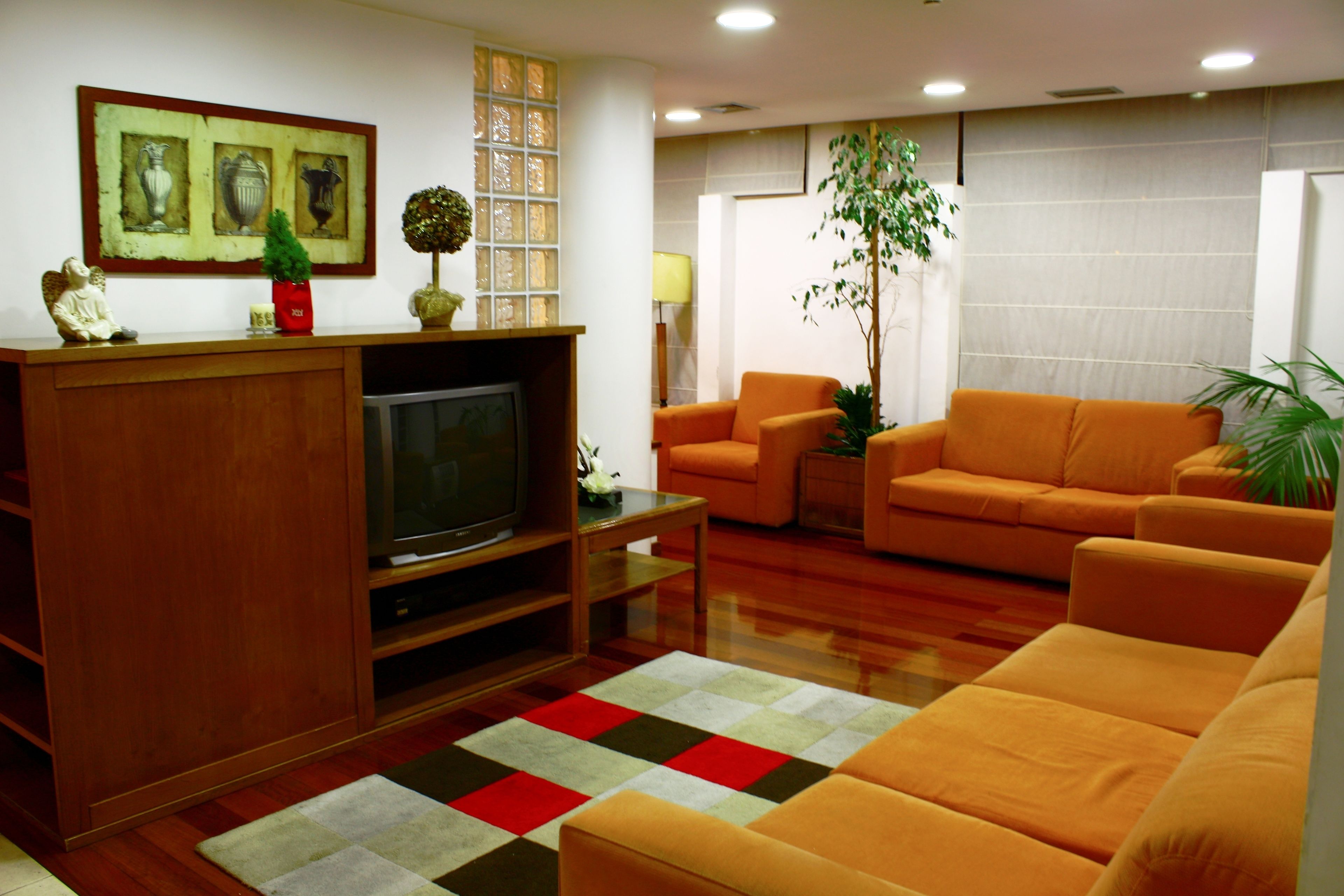 Uma sala de estar com televisão, sofás laranja, um rack de madeira e um tapete estampado.
