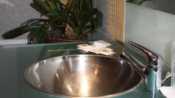 Casa de banho com lavatório de aço inoxidável, espelho e toalha pendurada num suporte.
