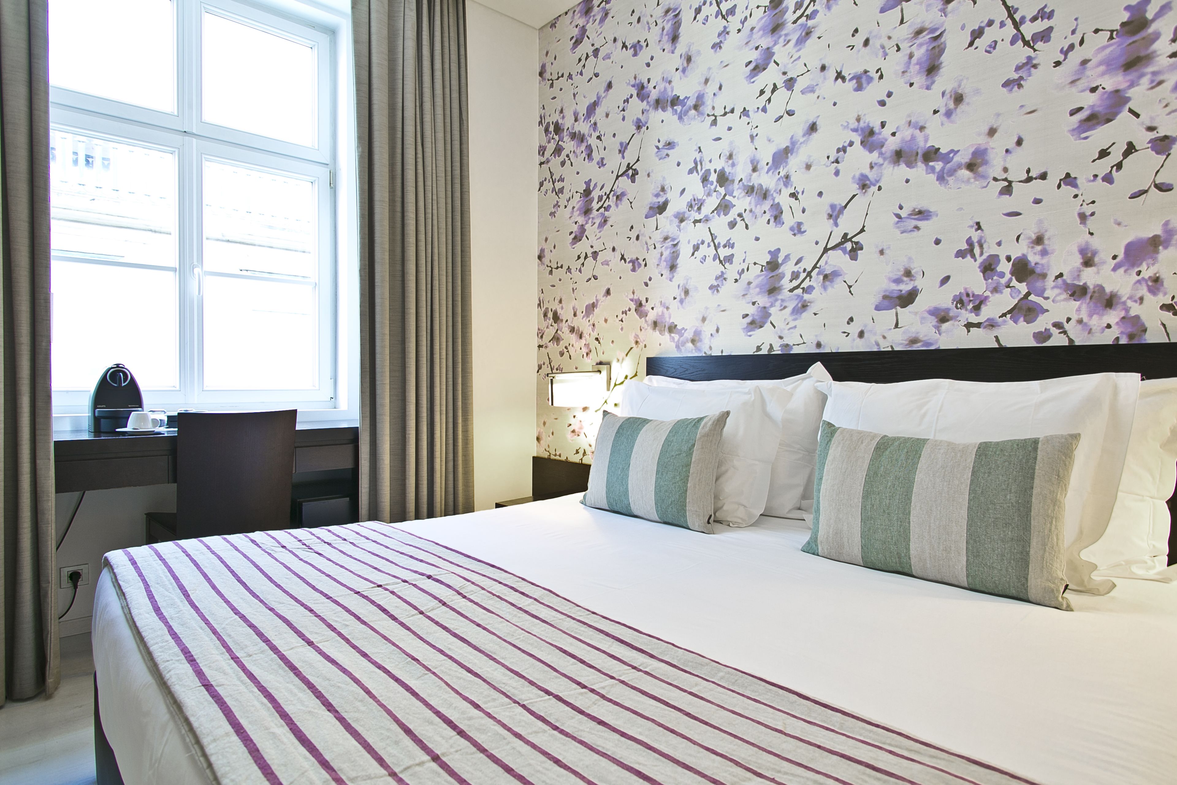 Quarto de hotel com cama, escrivaninha e janela.