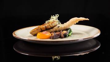 Um prato com diversos alimentos, incluindo um pedaço de carne, um vegetal e um item frito, tudo disposto sobre um prato de cerâmica.