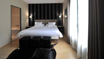 Quarto de hotel com uma cama grande, duas mesas de cabeceira com luminárias, um espelho e vista para o exterior.