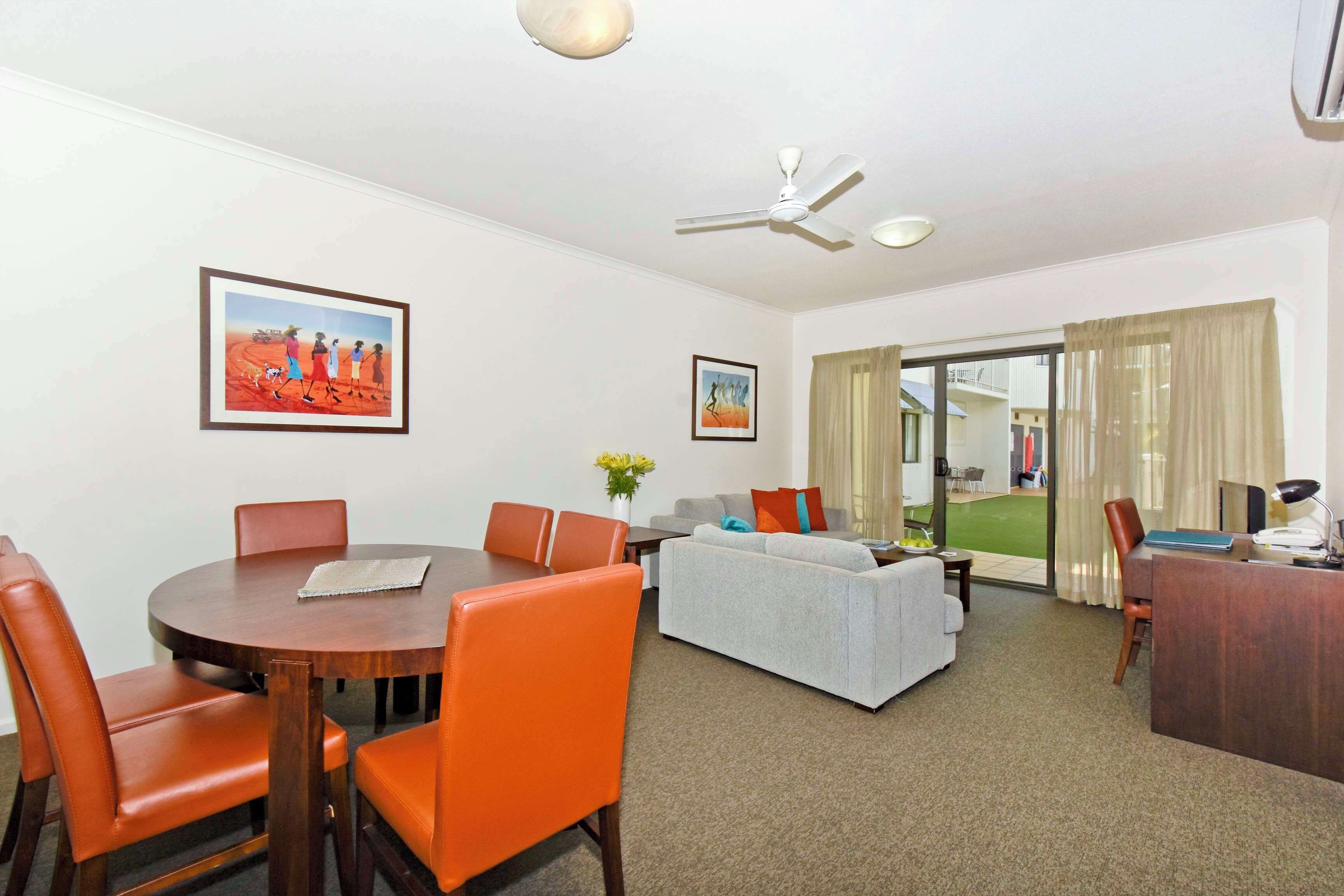 Quarto de hotel com área de refeições, sofá, escrivaninha e ventoinha no teto.