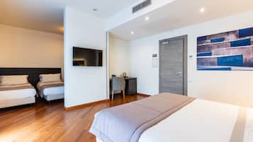 Quarto de hotel moderno com uma cama grande, duas camas menores, uma mesa e uma televisão.