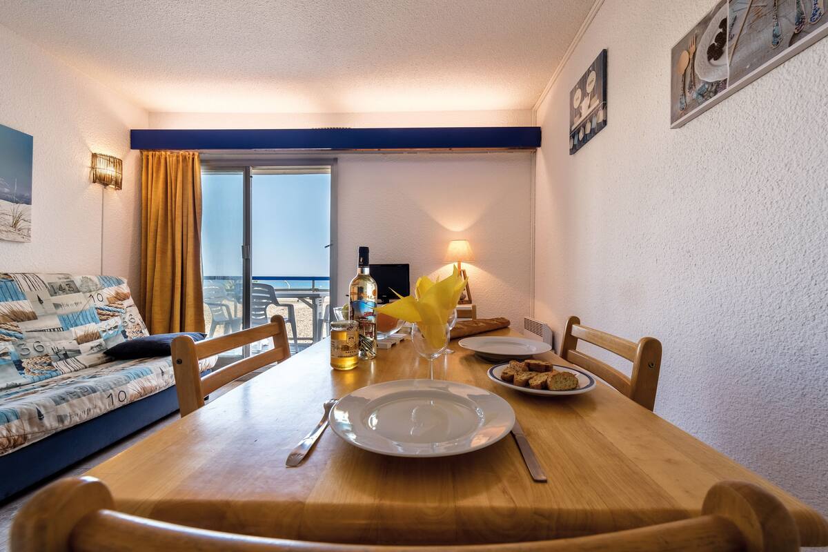 Uma sala de jantar com mesa de madeira, cadeiras, um sofá e vista para o exterior.