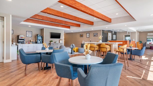 Um hall de hotel moderno com área de estar central, balcão de recepção e cozinha ao fundo.