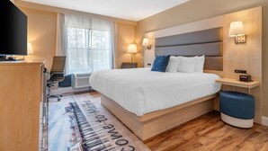 Quarto de hotel moderno com uma cama grande, uma mesa de escritório com um computador, uma cadeira, uma janela com cortinas e uma luminária na parede.