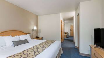 Quarto de hotel com uma cama grande, uma televisão sobre uma cômoda de madeira, e um corredor que leva a outro quarto.