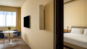 Quarto de hotel com cama, televisão na parede, mesa com cadeiras e janela com cortinas.