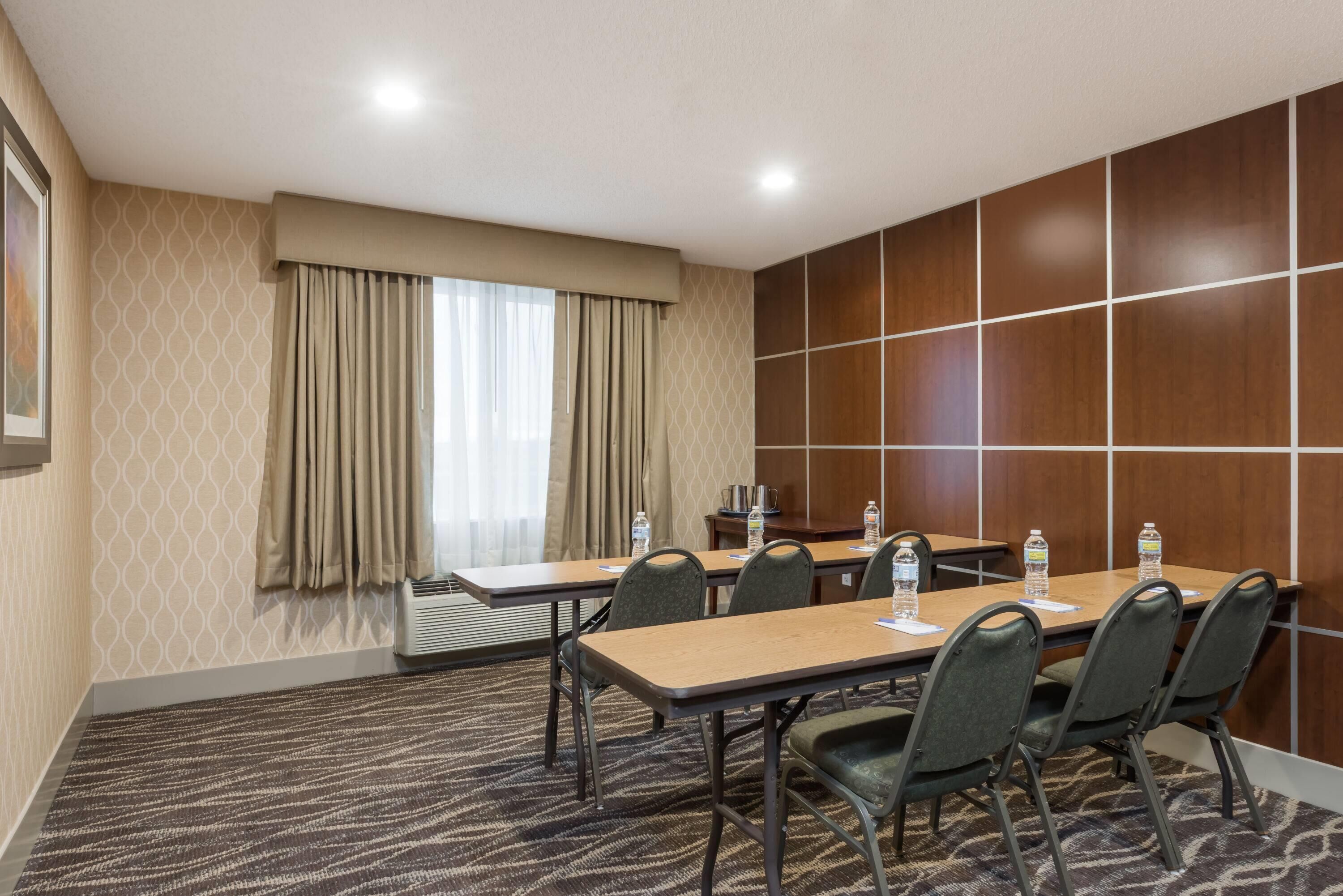 Uma sala de conferência com uma mesa comprida, cadeiras e uma janela com cortinas.