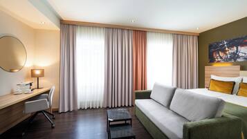 Quarto de hotel com uma cama, um sofá, uma escrivaninha com cadeira e uma mesinha.