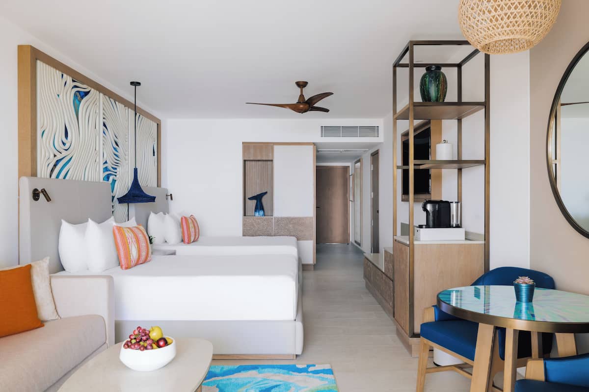 Quarto de hotel moderno com cama, sofá, mesa de jantar e cozinha compacta.