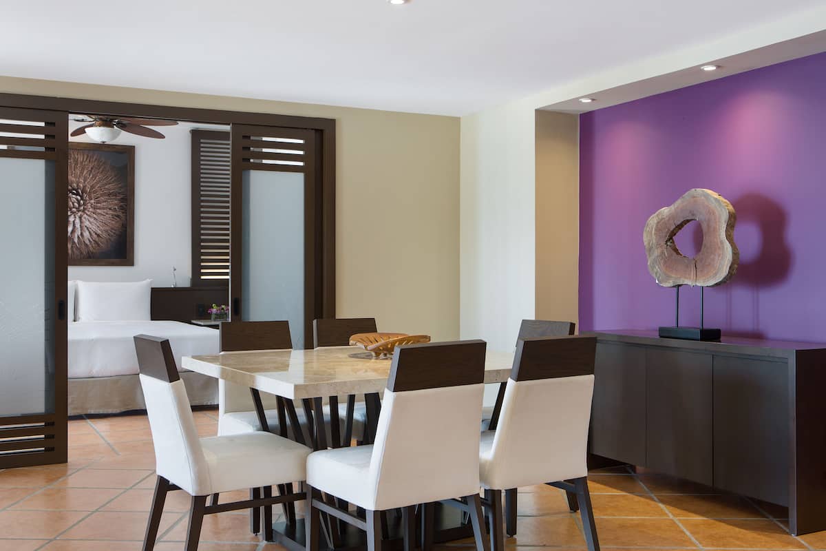 Uma área de refeições com mesa e cadeiras, uma cama e uma parede roxa com um objeto decorativo.
