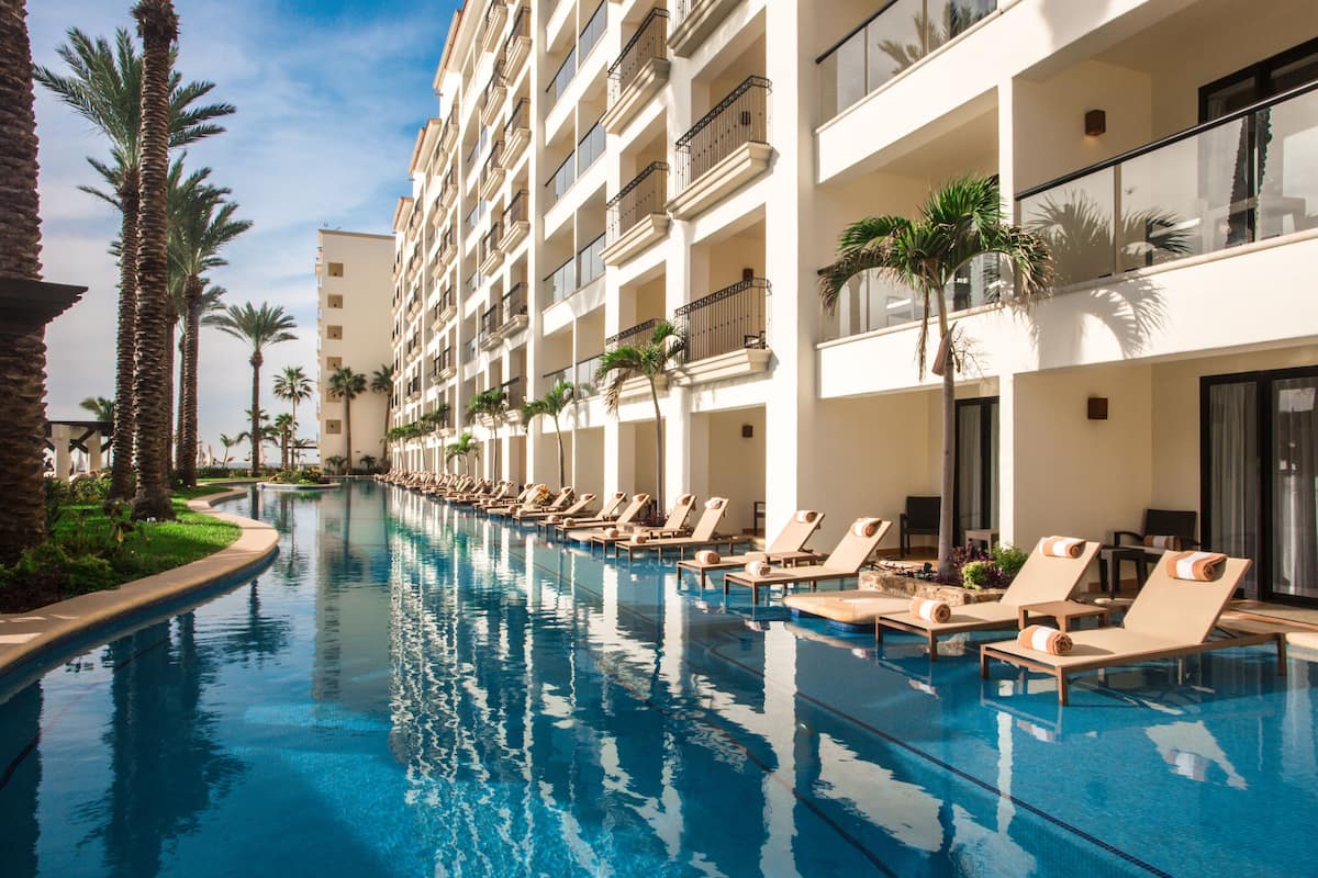 Área de piscina de hotel com espreguiçadeiras e palmeiras.