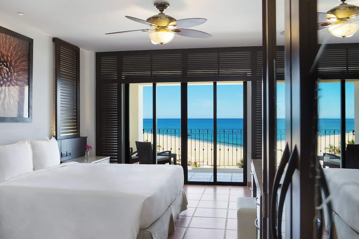 Quarto de hotel com cama, escrivaninha e vista para a praia.