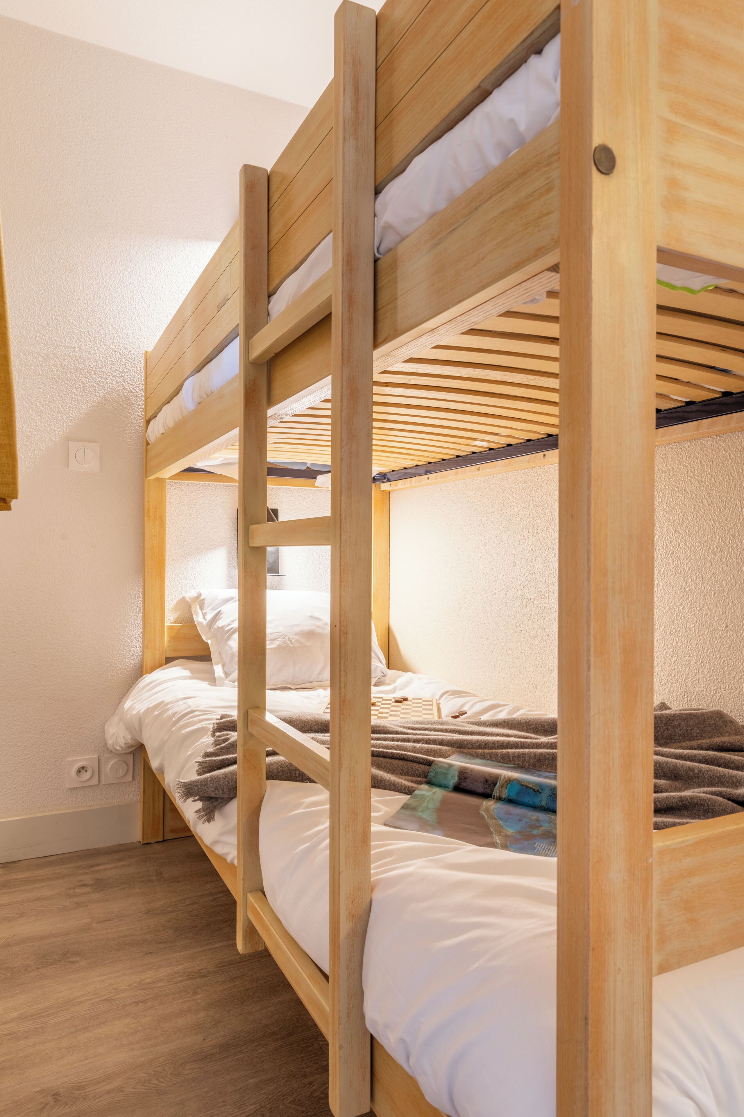 Quarto com beliches de madeira, roupa de cama branca e chão de madeira.