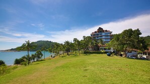Um hotel com um amplo gramado, palmeiras e vista para o mar.