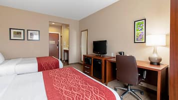Quarto de hotel com duas camas, uma escrivaninha com computador, televisão e luminária.